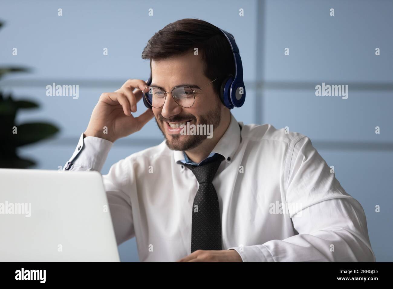 Happy businessman listening using headphones looking at laptop screen ...