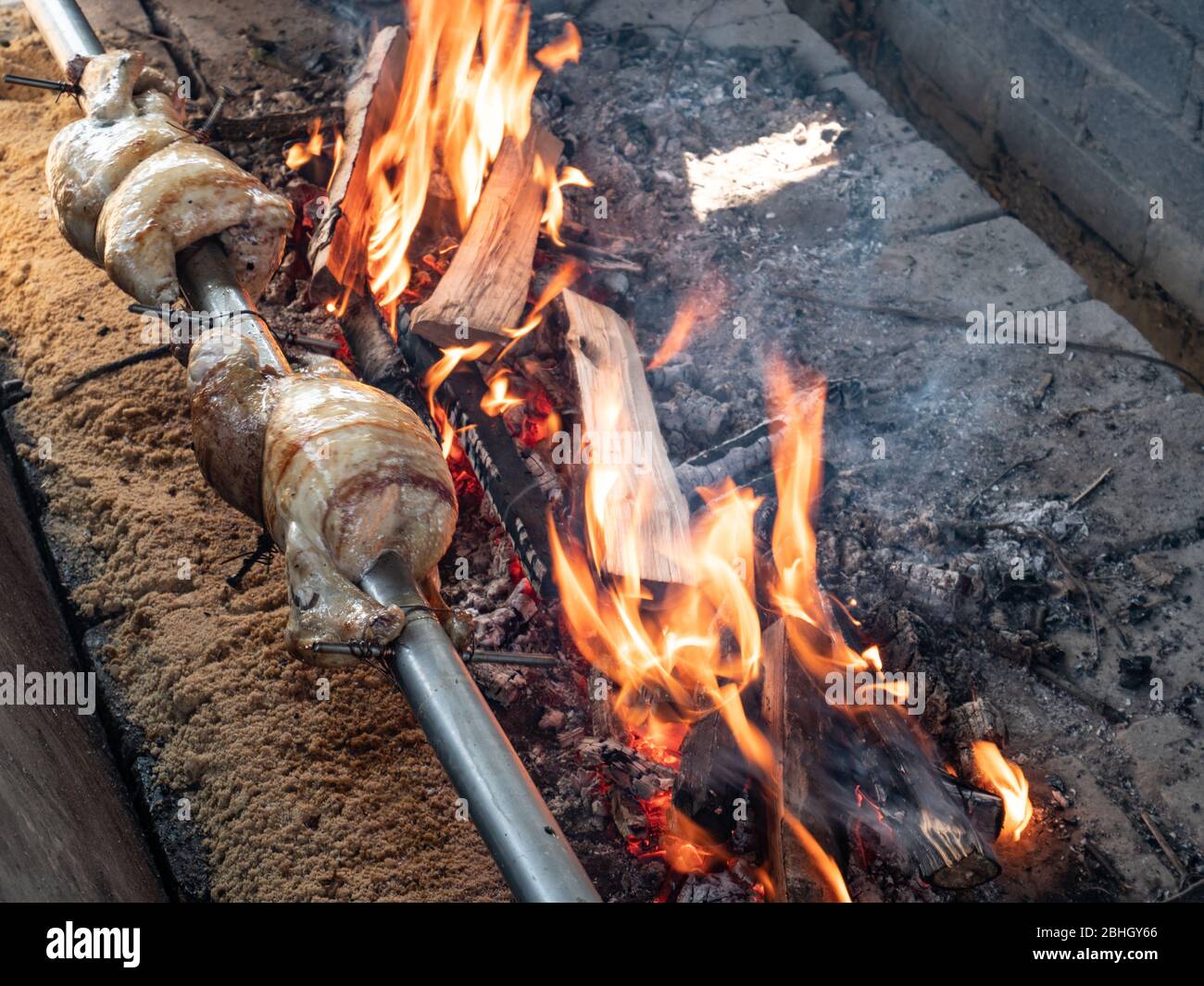 Chicken roasted on spit being grilled over the bright glowing beech ...