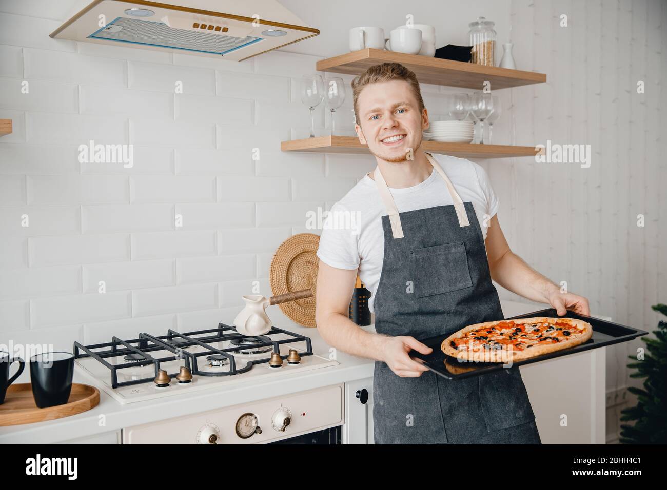 European male chef smiles and holds baking tray with hot Italian pizza ...