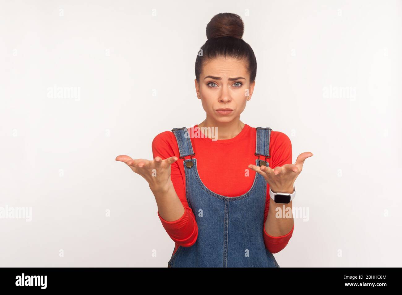 What do you want? Portrait of embarrassed girl with hair bun in denim ...