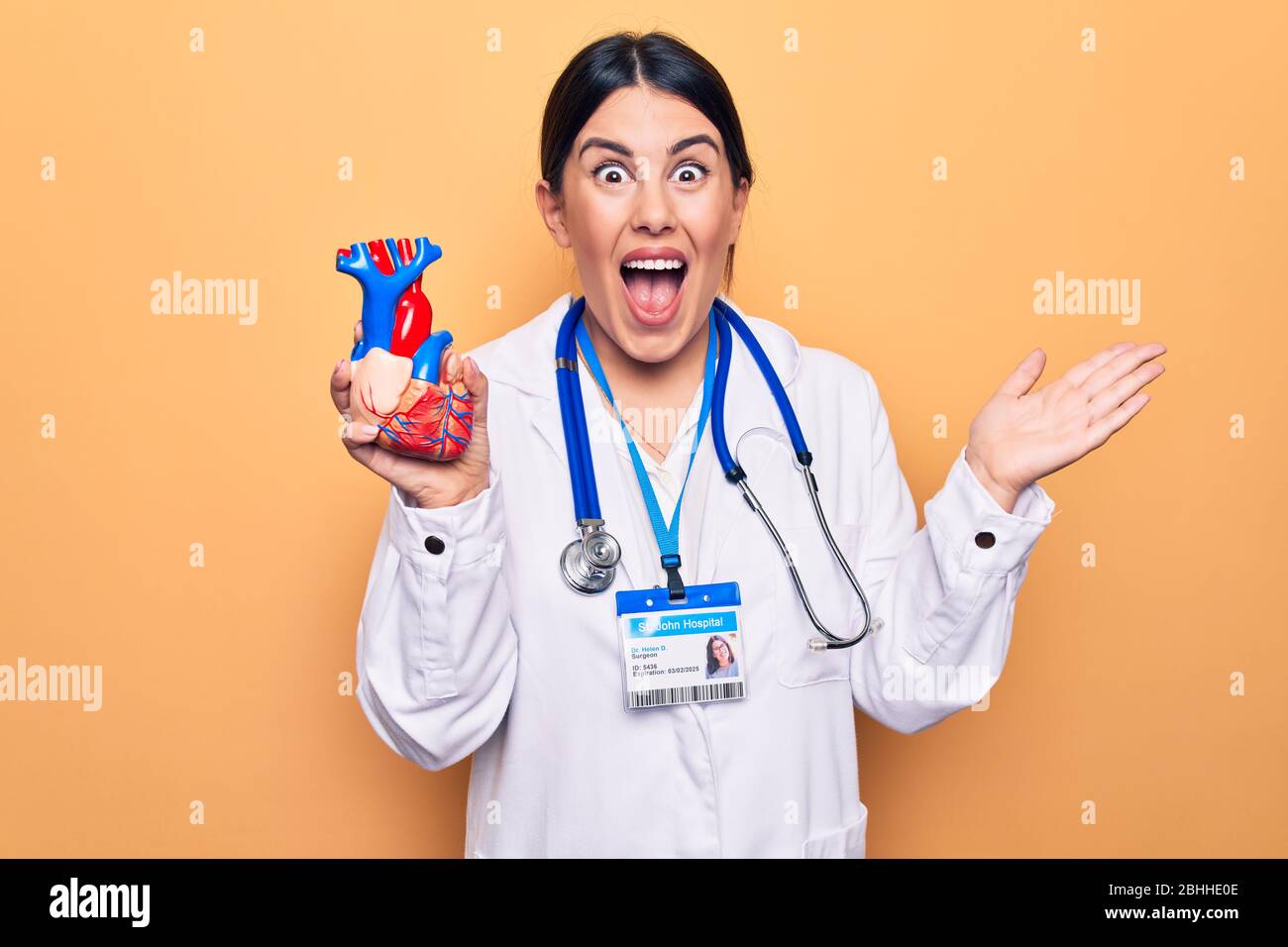 Young beautiful cardiologist woman wearing stethoscope holding heart ...
