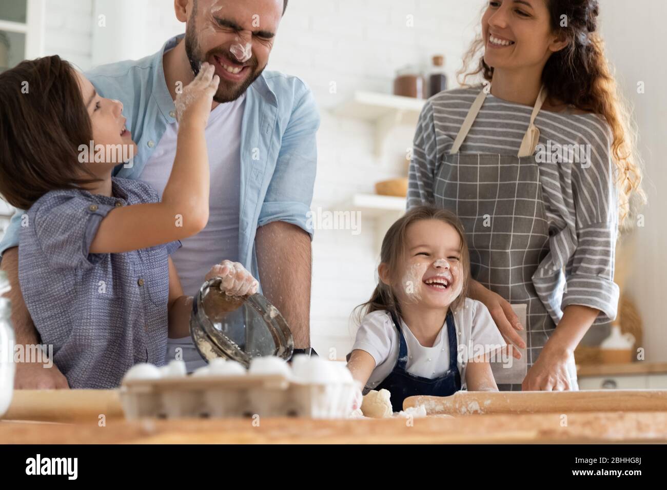 Overjoyed small children siblings spreading flour on laughing parents ...