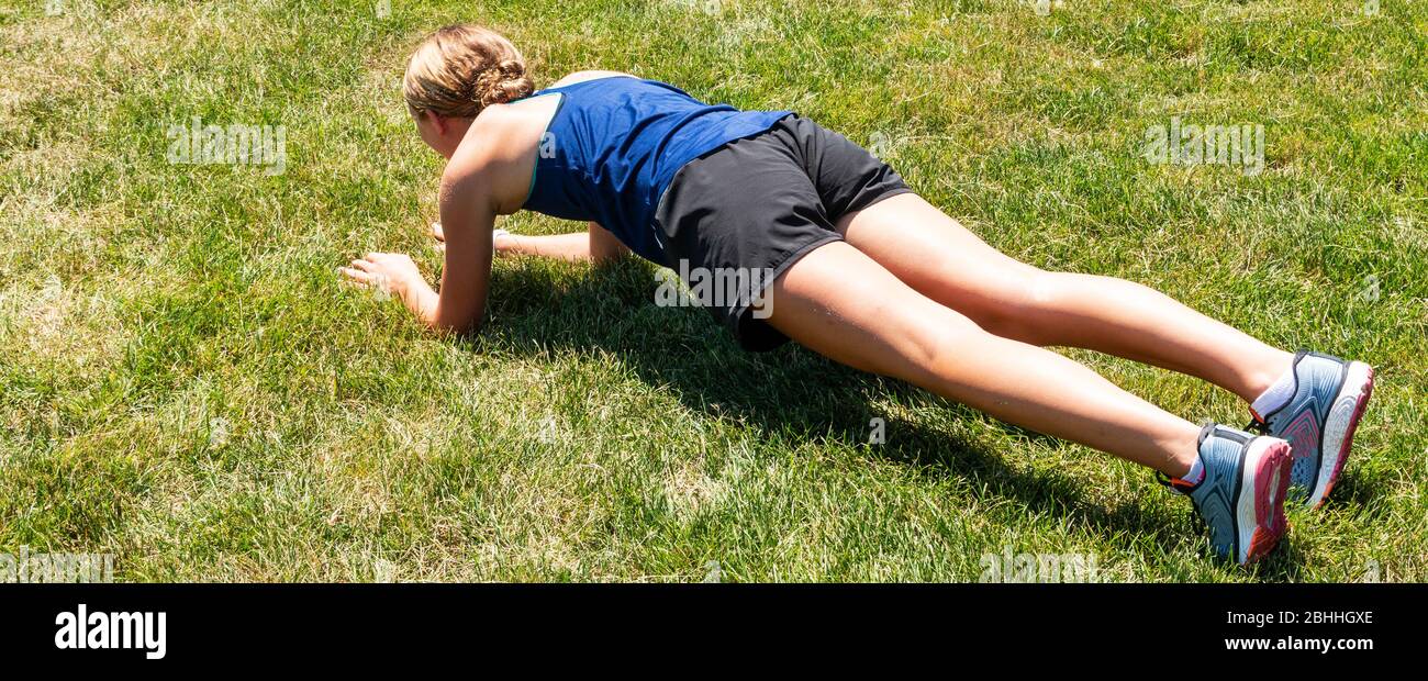 High school girl on her elbows holding a front plank on green grass ...