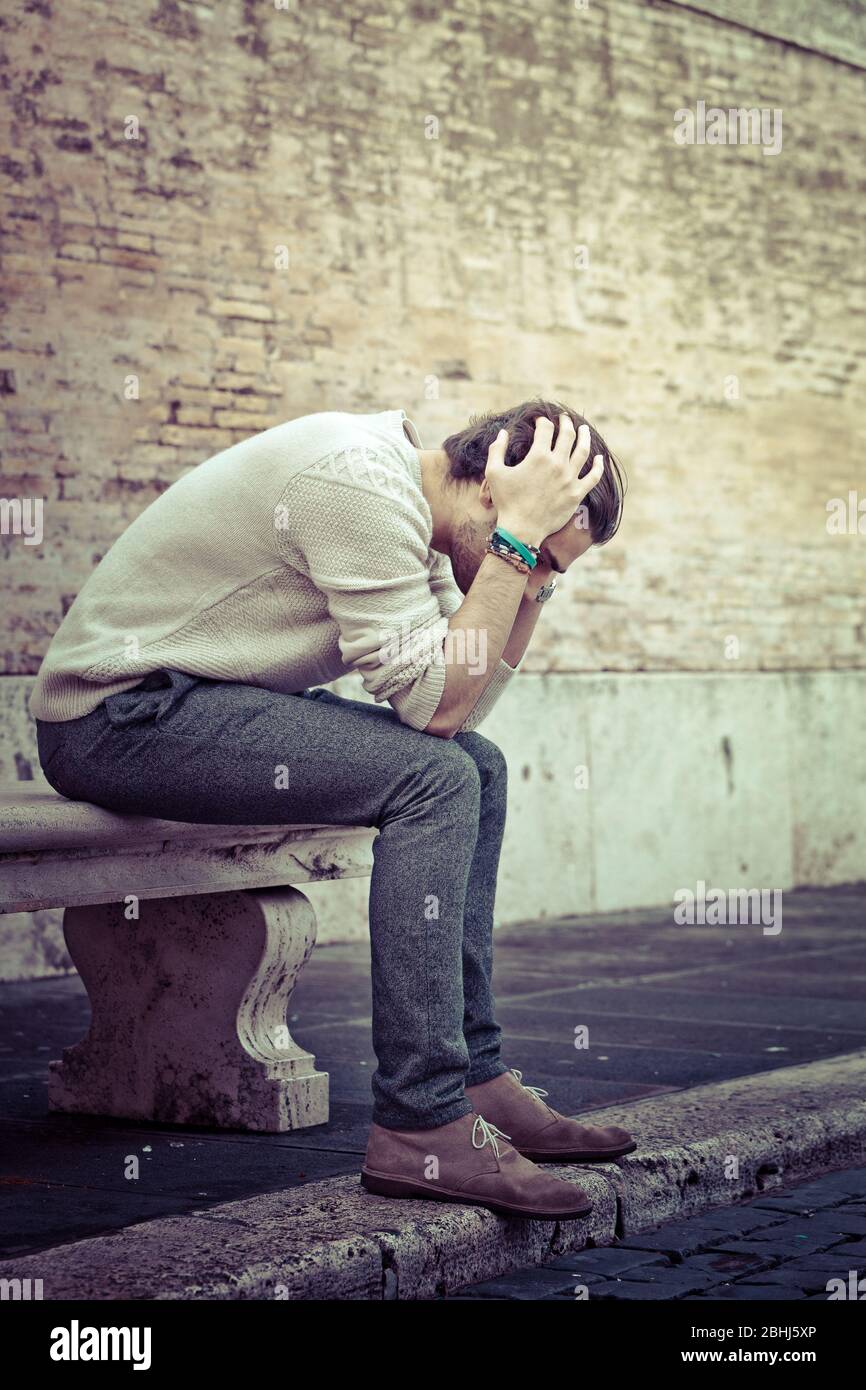 Young worried man sitting and staring outdoors with hands on the head ...
