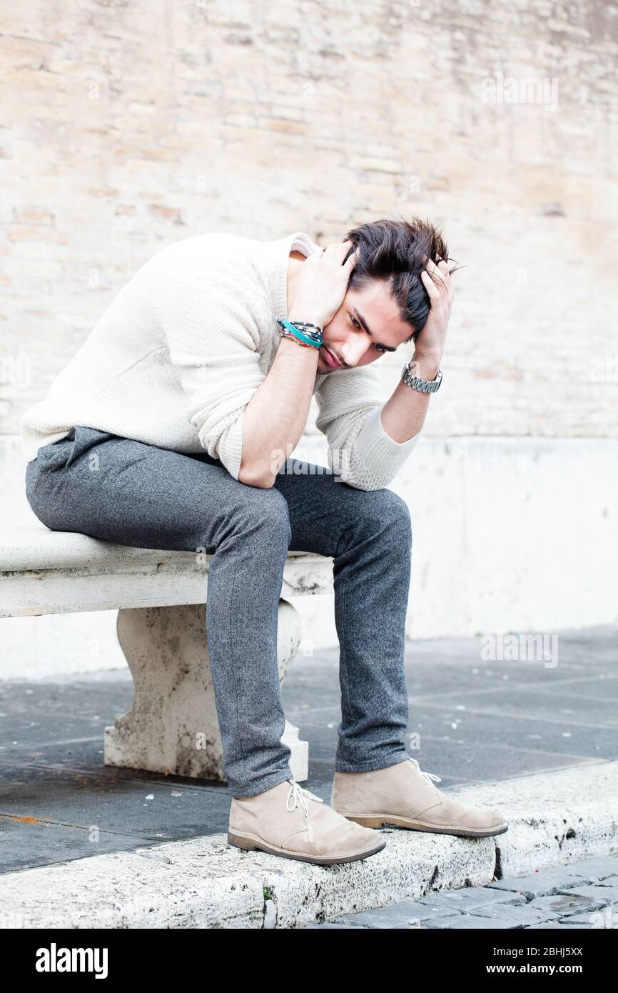 Young worried man sitting and staring outdoors with hands on the head ...