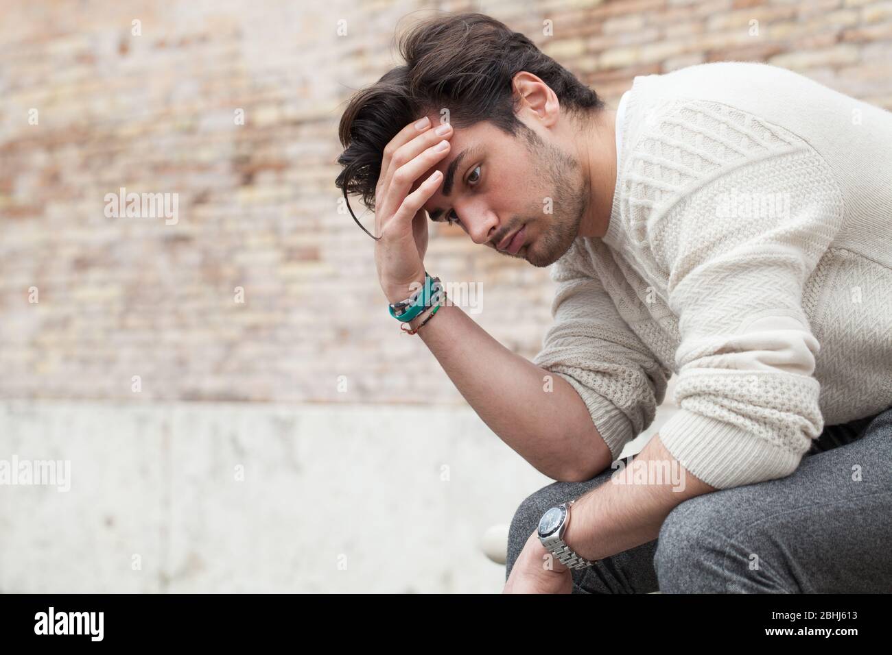Young worried man sitting and staring outdoors with hands on the head ...