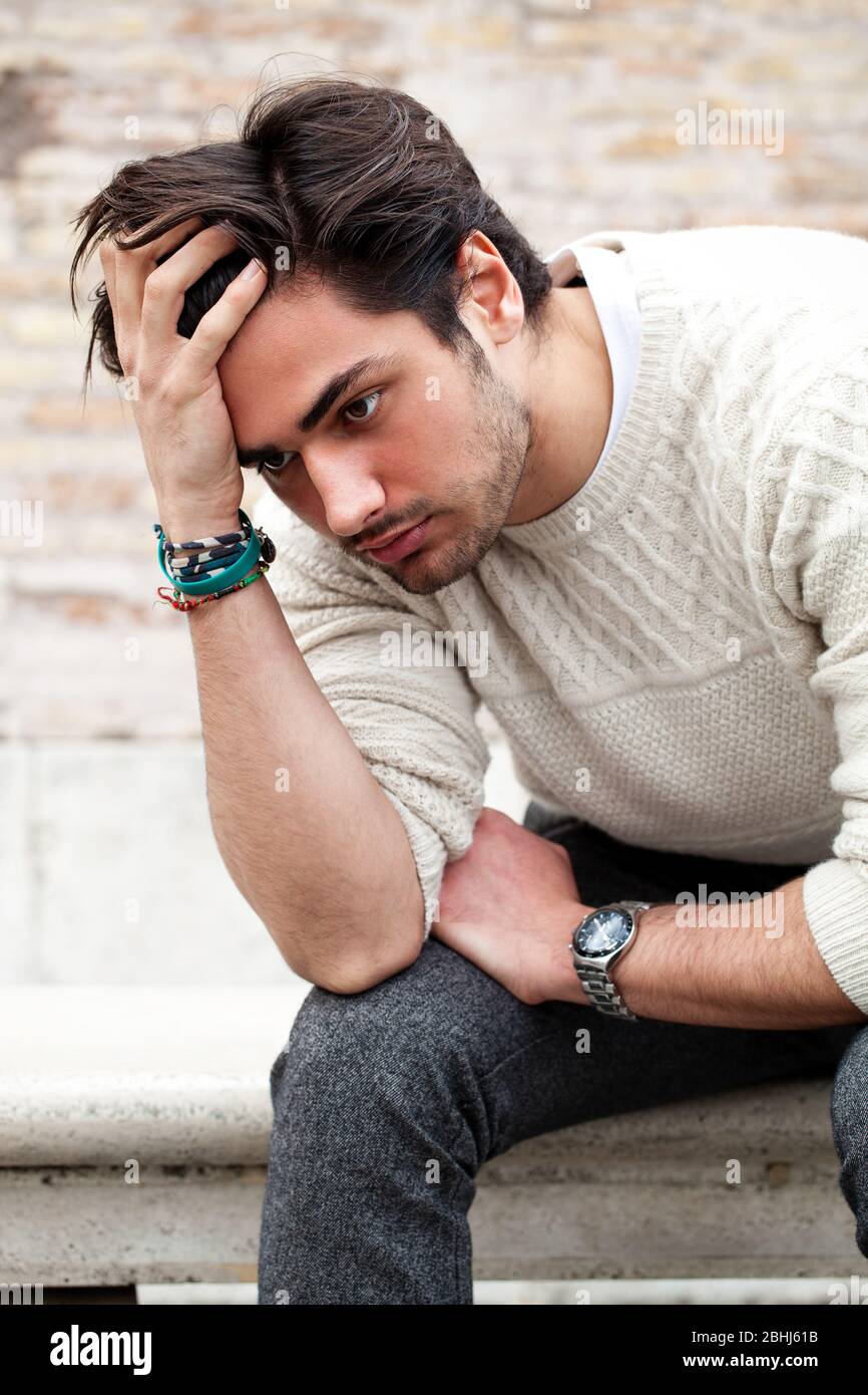 Young worried man sitting and staring outdoors with hands on the head ...
