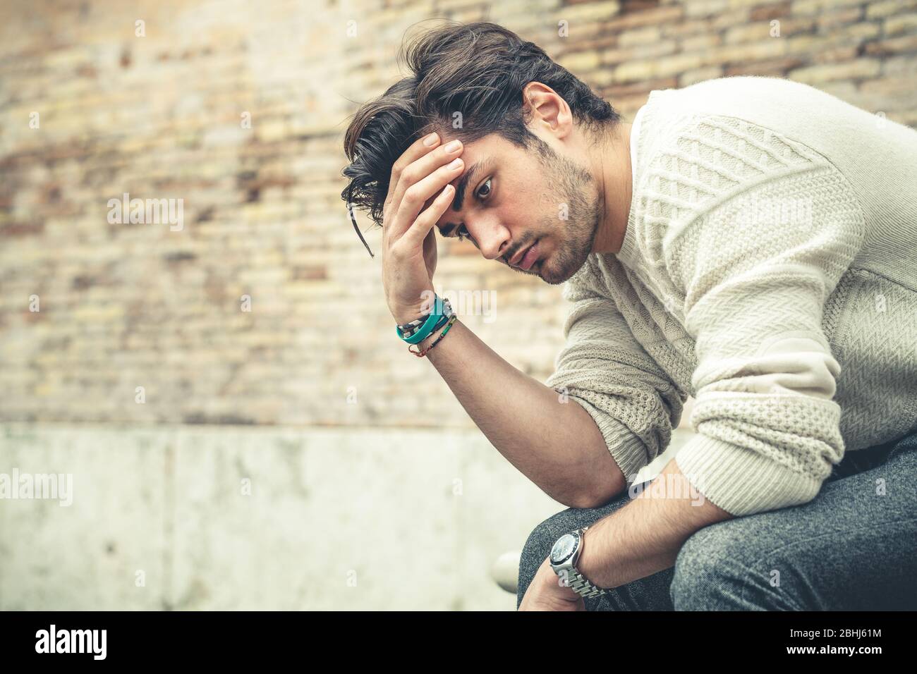 Young worried man sitting and staring outdoors with hands on the head ...