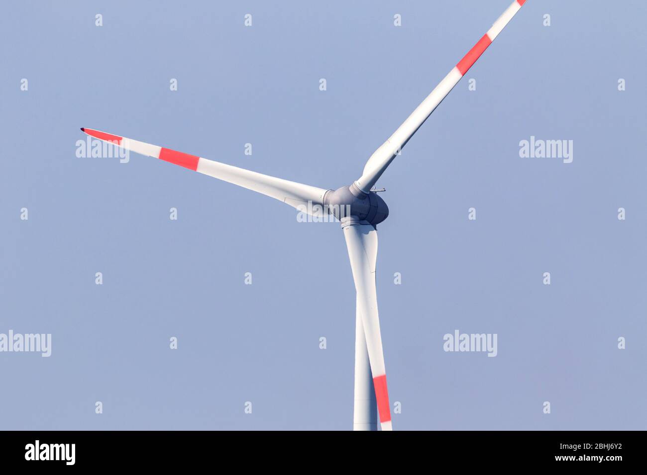 A closeup portrait of a white wind turbine in a blue sky with red ...