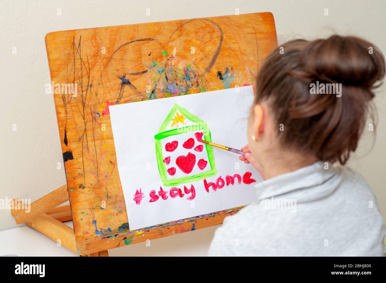 Stay Home concept. Child is drawing house with red hearts on the sheet ...