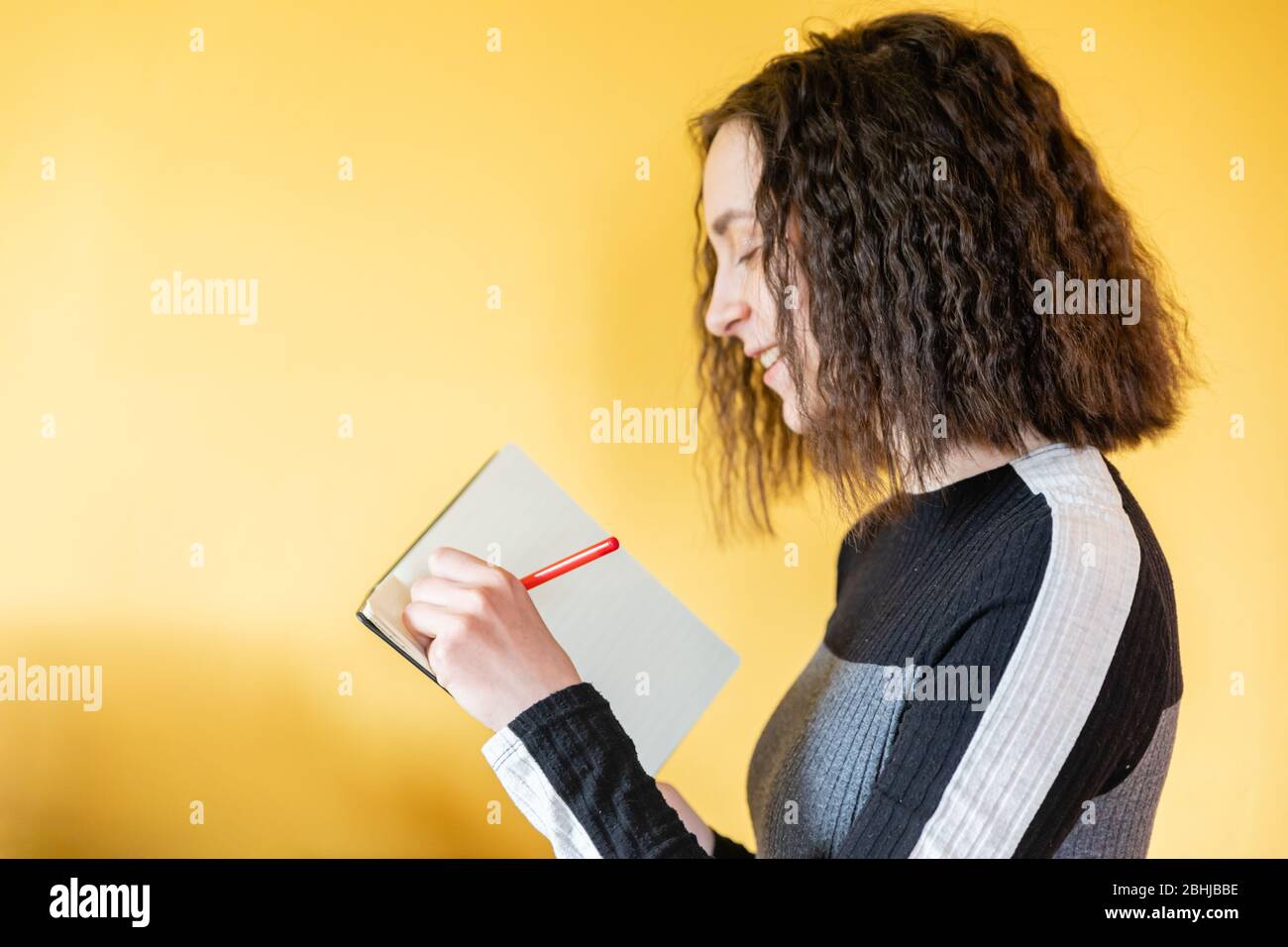 Young caucasian girl with short curly dark hair writing in notepade ...