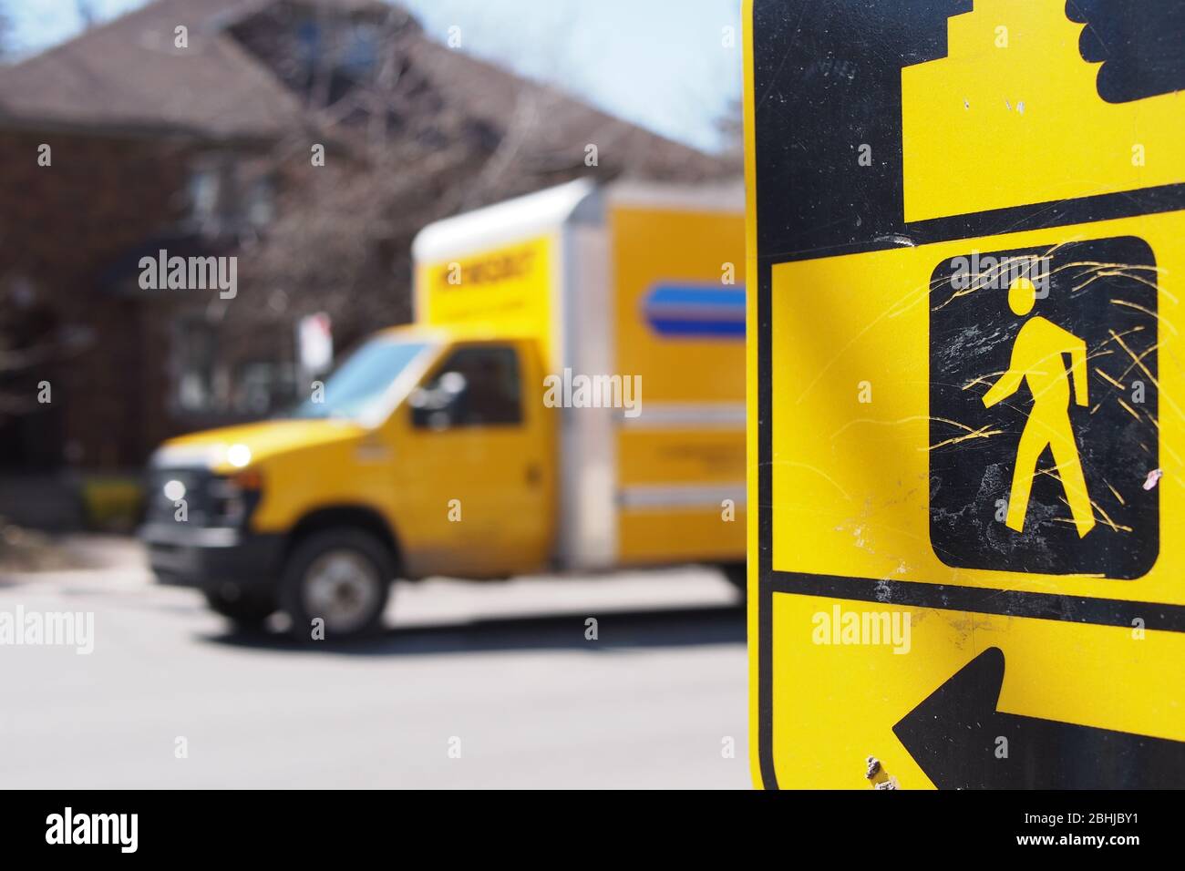 A yellow (Penske) rental box (cube) van behind a yellow crosswalk sign ...