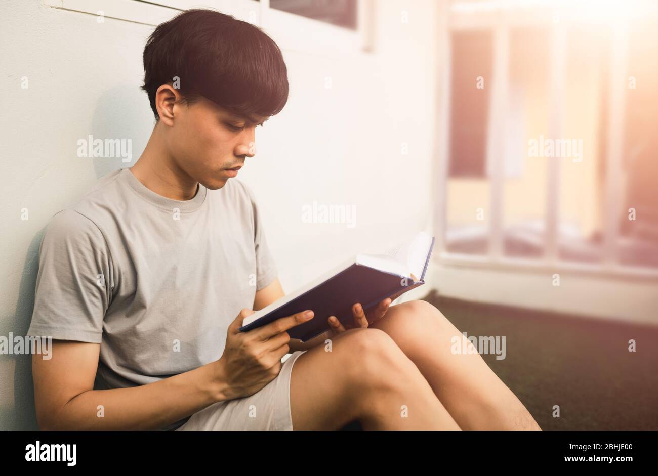 Young handsome asian man reading book at room balcony in free time from ...