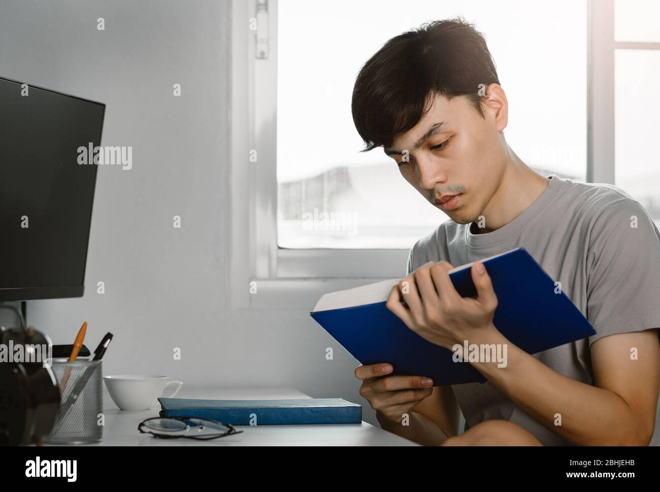 Young handsome asian man reading book at work desk in free time from ...
