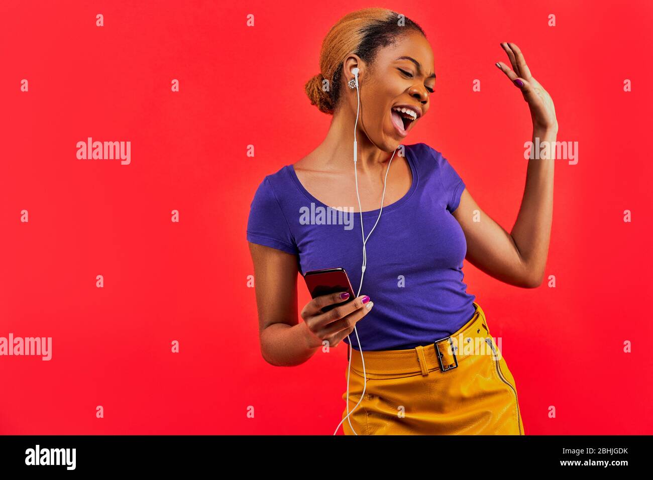 Joyful girl in wired headphones is dancing with a smartphone in her ...