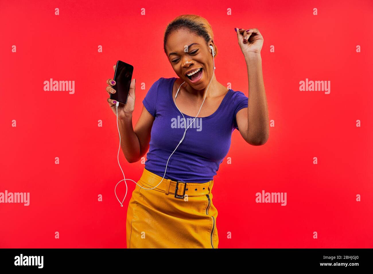 Joyful girl in wired headphones is dancing with a smartphone in her ...