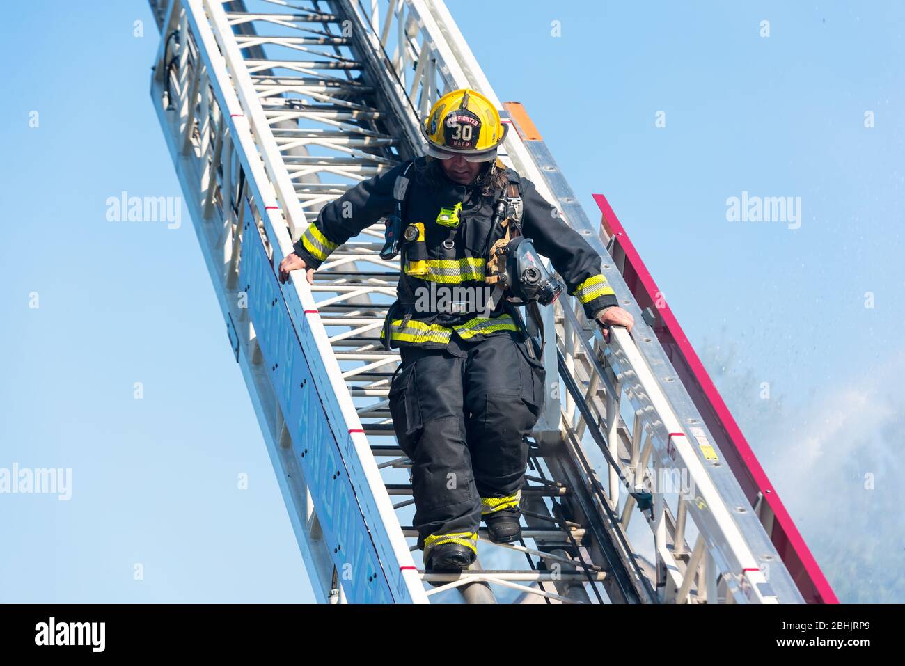 Uniformed firefighter descending a ladder while fighting a fire Stock ...
