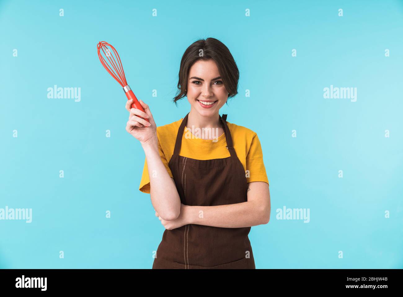 Image of cute cheery young woman chef holding whisk isolated over blue ...