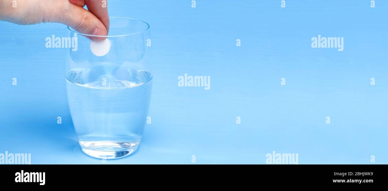 Effervescent instant tablet in a hand over a glass of water on a blue ...