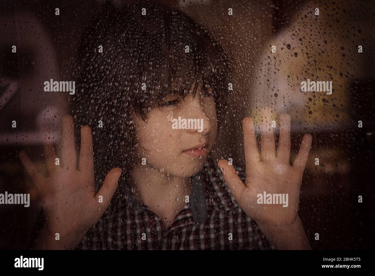 Sad boy behind the glass in raindrops Stock Photo - Alamy