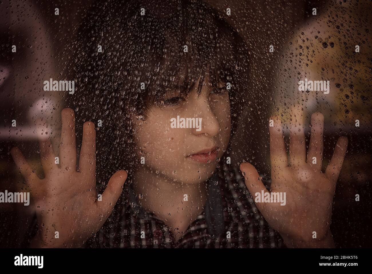 Sad boy behind the glass in raindrops Stock Photo - Alamy