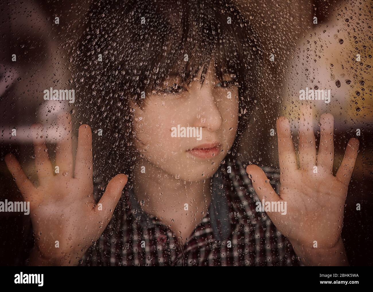 Sad boy behind the glass in raindrops Stock Photo - Alamy