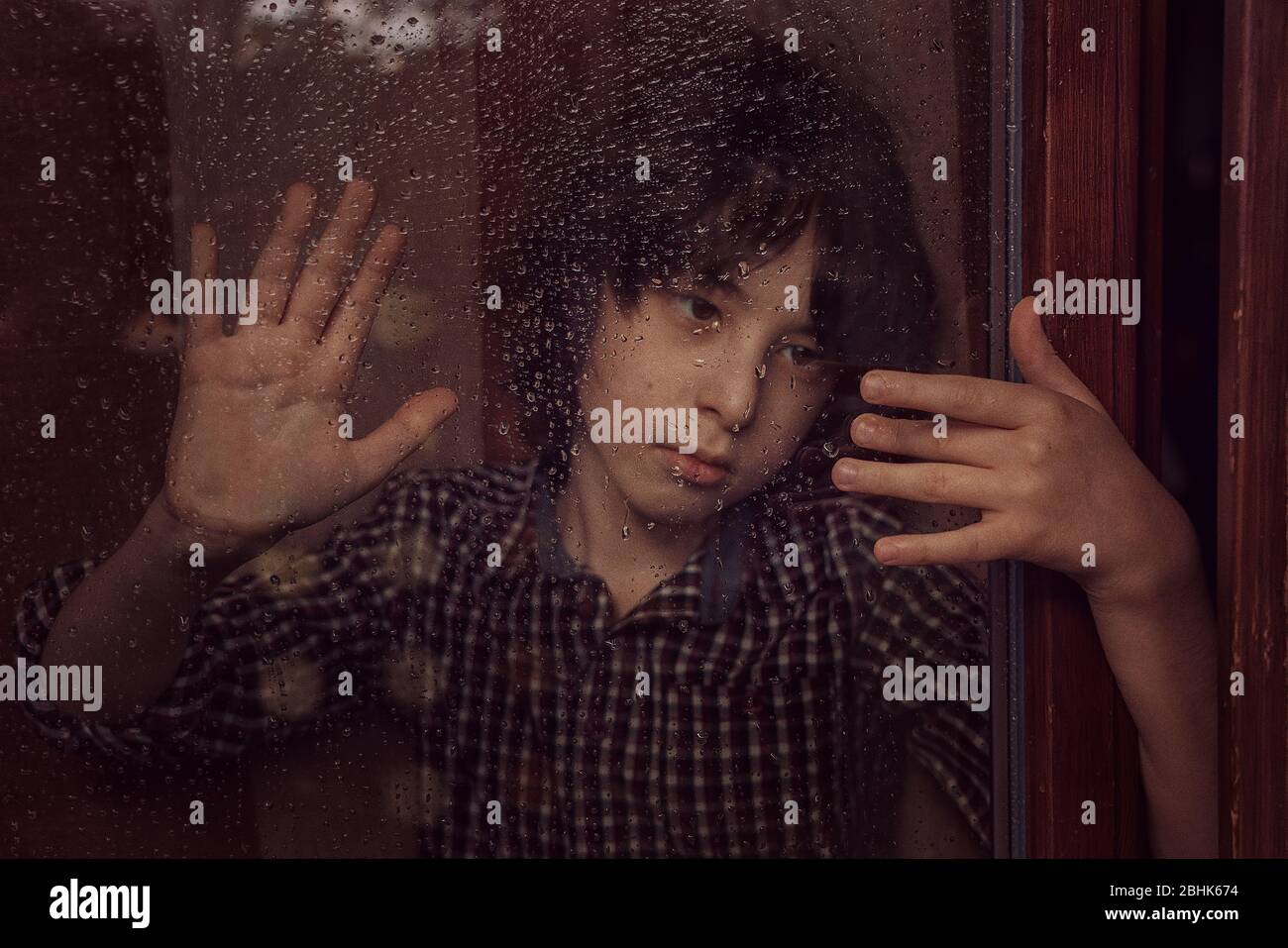 Sad boy behind the glass in raindrops Stock Photo - Alamy
