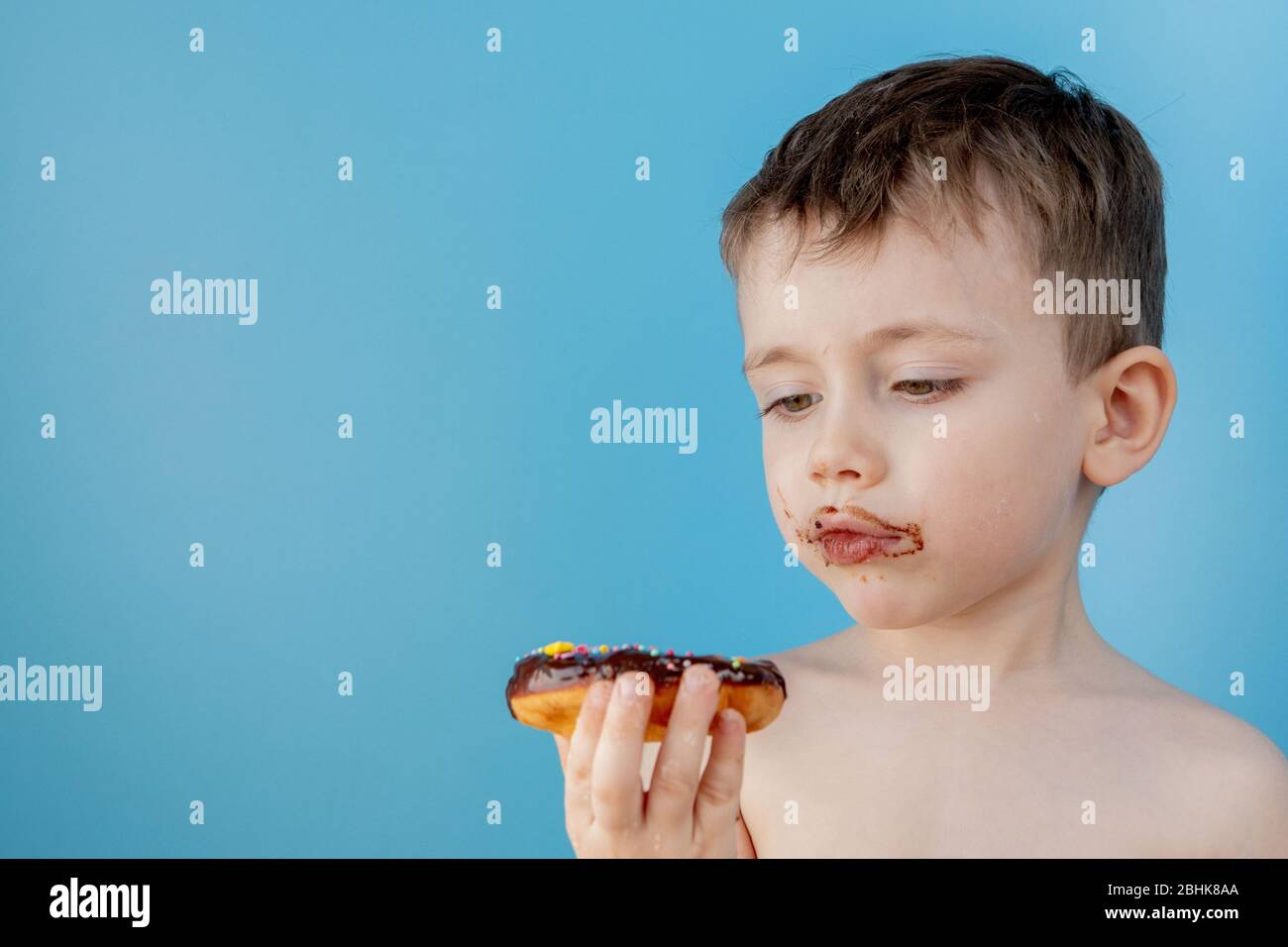 Little boy eating donut chocolate on blue background. Cute happy boy ...