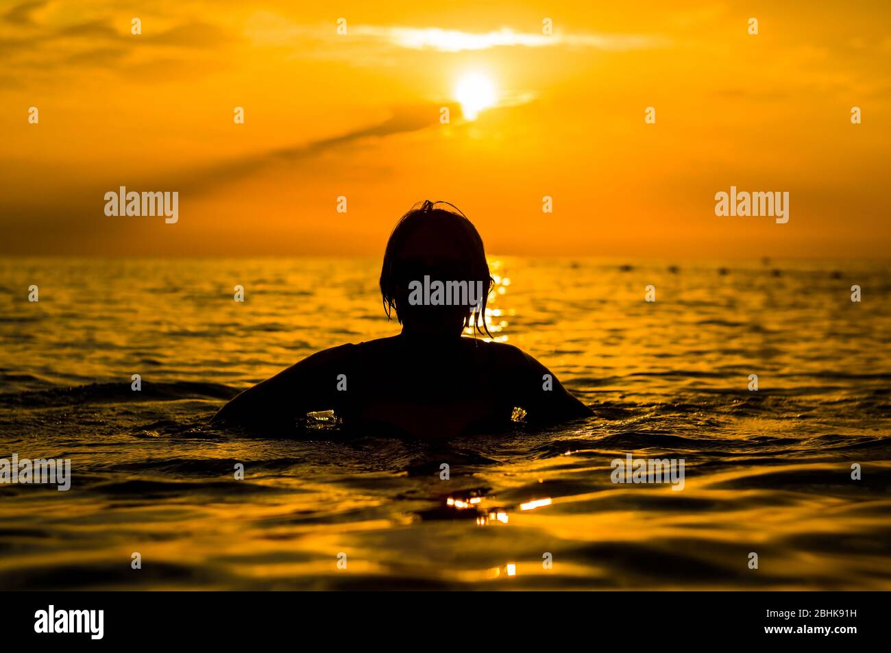 Girl swimming in the sea at sunset, splashes of transparency water ...