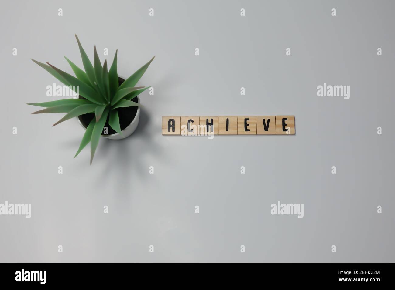 The word Achieve is written in wooden letter tiles on a white ...