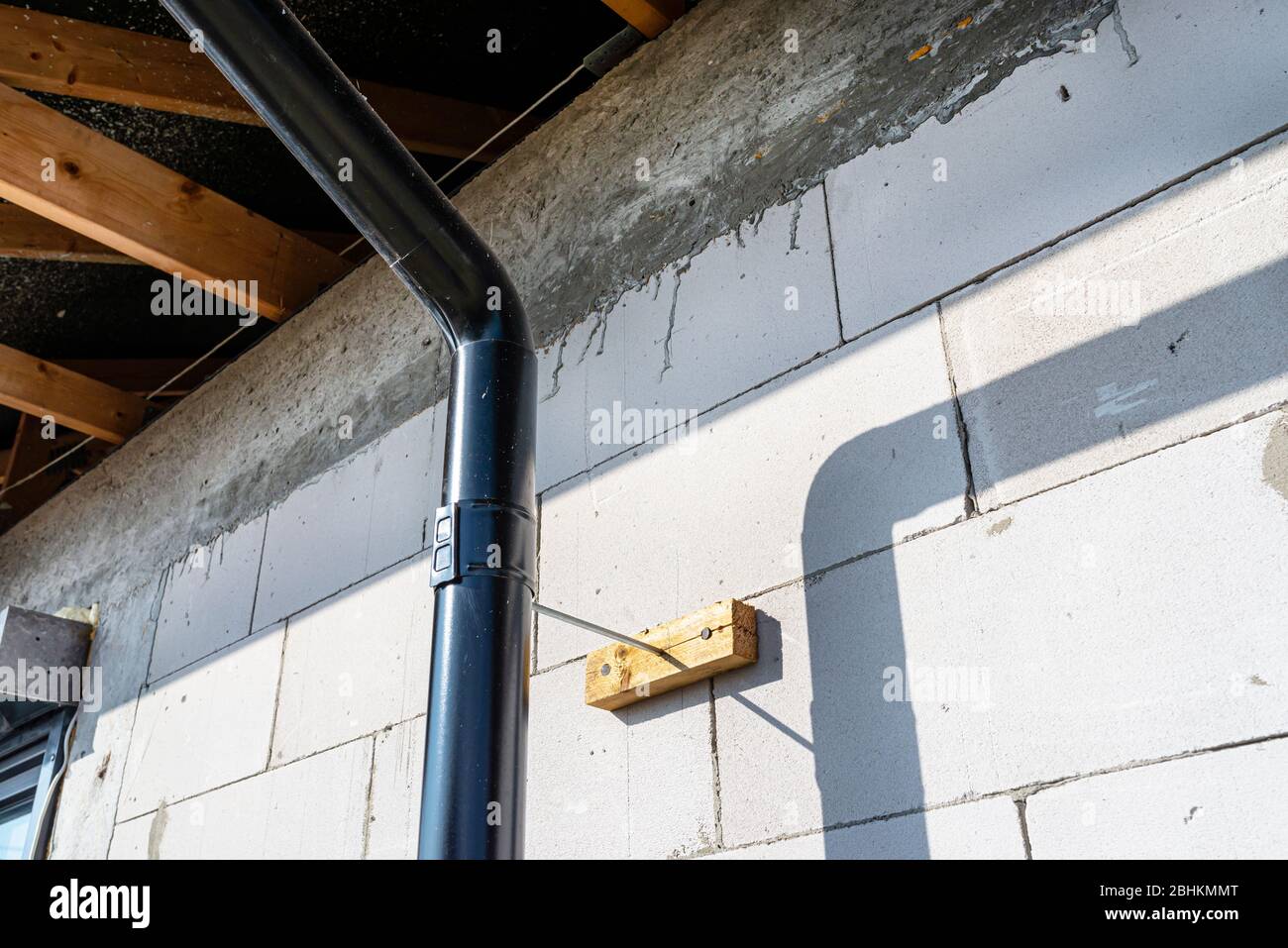 A black metal gutter attached to the raw wall of the house to make a ...