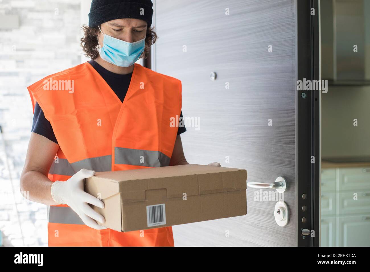 Young delivery man at front door with a parcel box, wearing gloves and ...