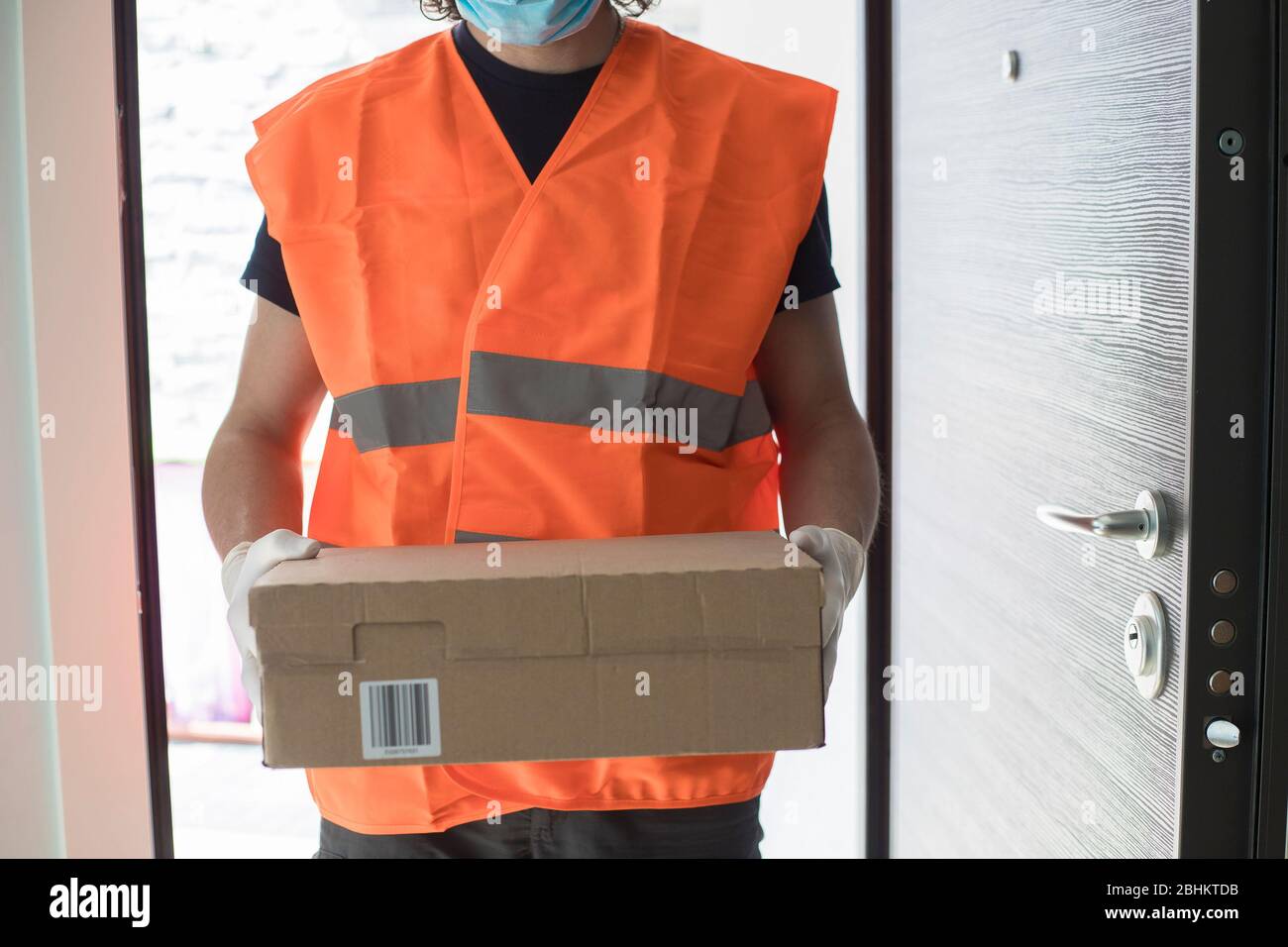 Young delivery man at front door with a parcel box, wearing gloves and ...