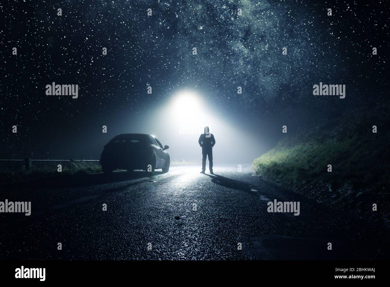 A lone car, parked on the side of the road with a hooded figure, on a ...