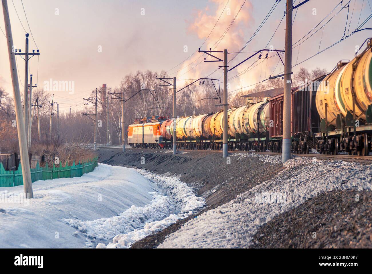 freight train leaving a bend, trees behind an industrial area, winter ...