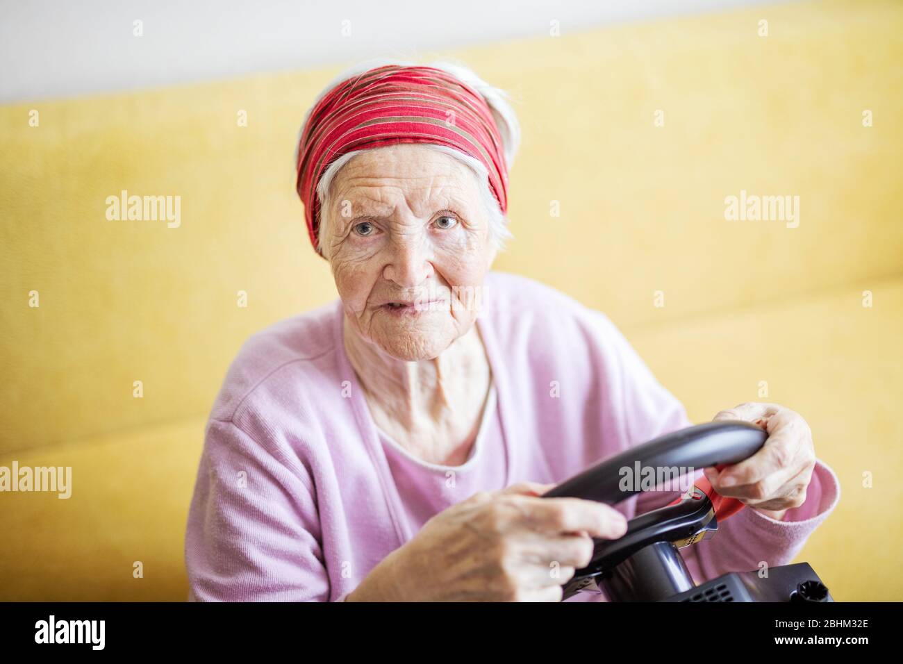 Senior woman enjoying car racing video game while sitting on couch at ...