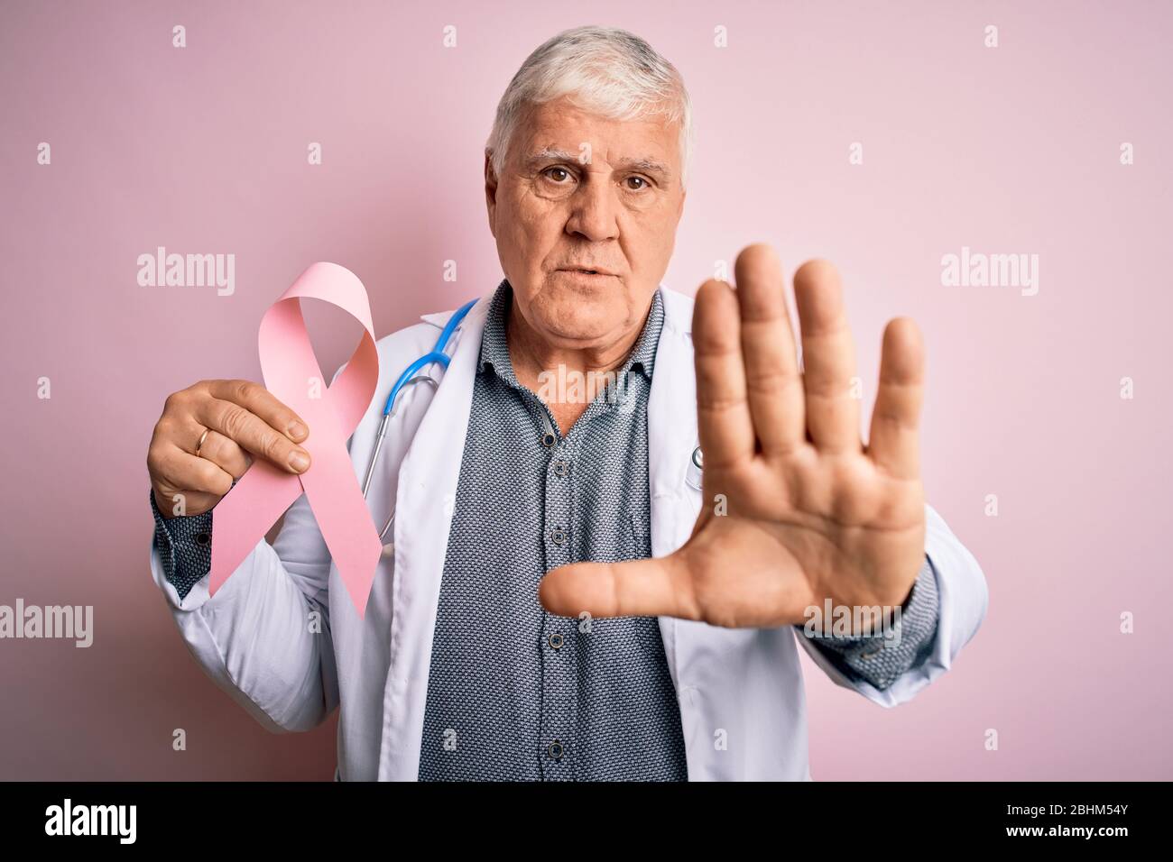 Senior handsome hoary doctor man wearing stethoscope holding pink ...