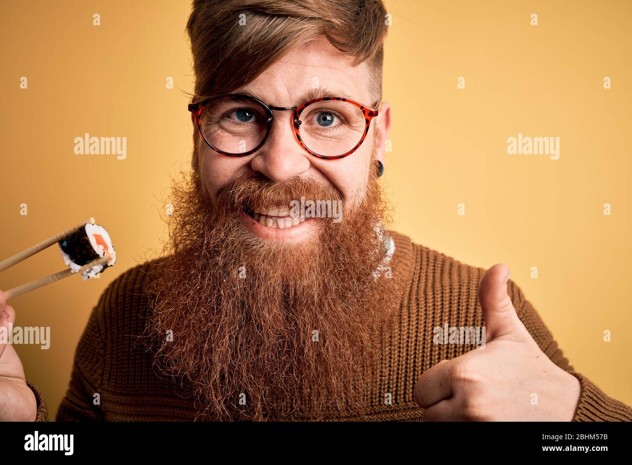 Redhead Irish Man With Beard Eating Salmon Maki Sushi Using Chopsticks Over Yellow Background