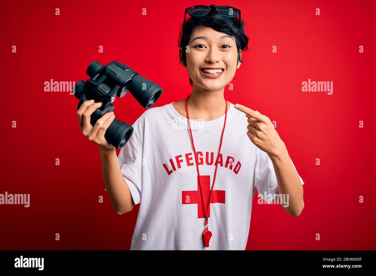 Young beautiful asian lifeguard girl using whistle and binoculars over ...