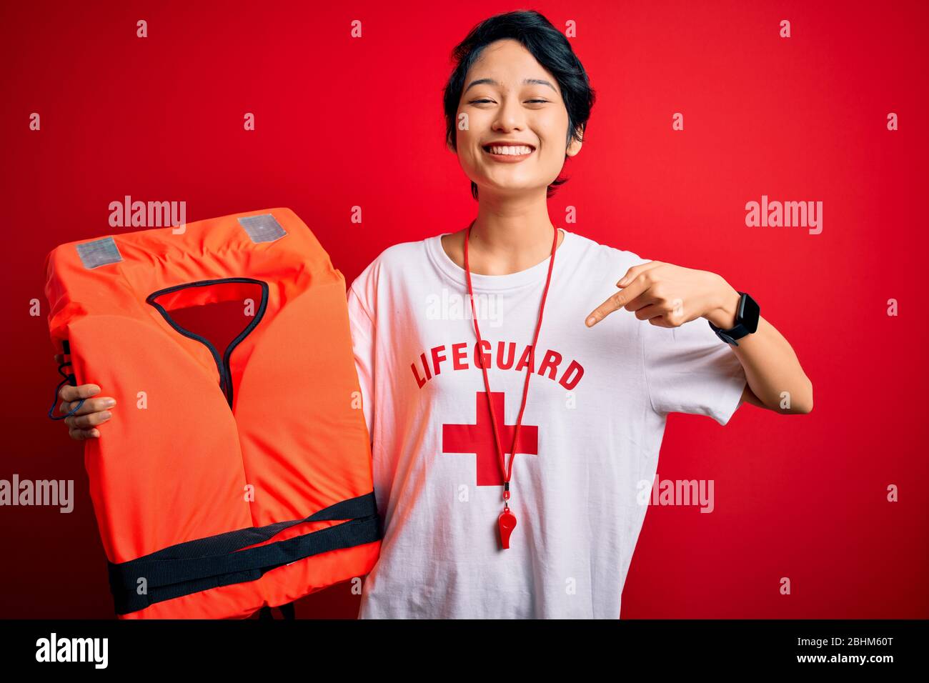 Young beautiful asian lifeguard girl using whistle holding orange life ...
