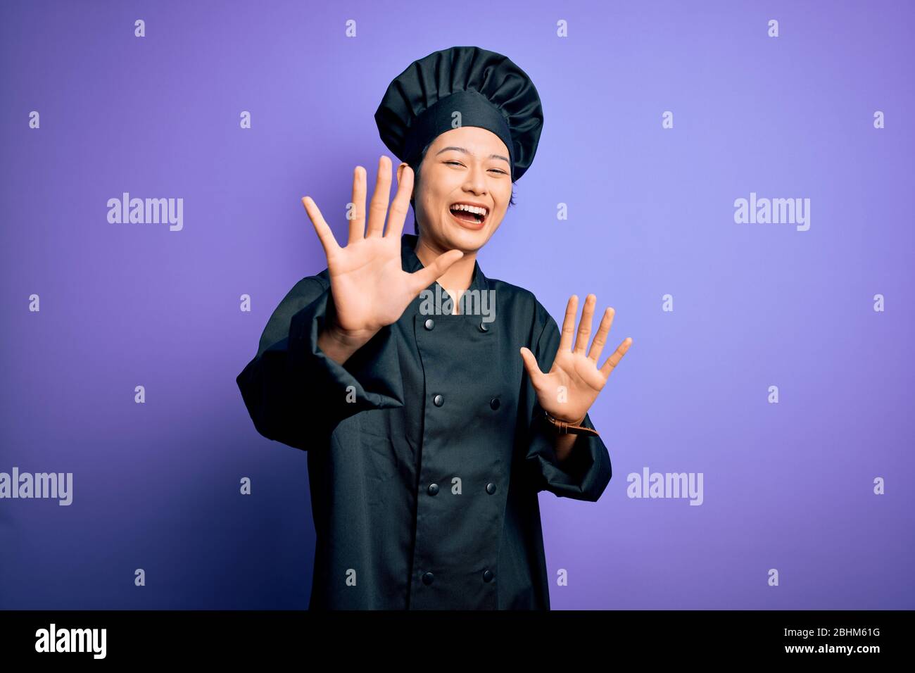 Young beautiful chinese chef woman wearing cooker uniform and hat over ...