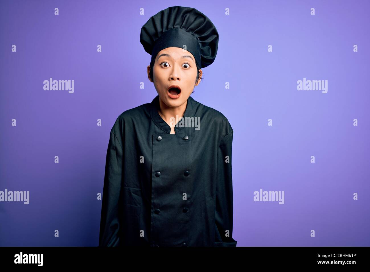 Young beautiful chinese chef woman wearing cooker uniform and hat over ...