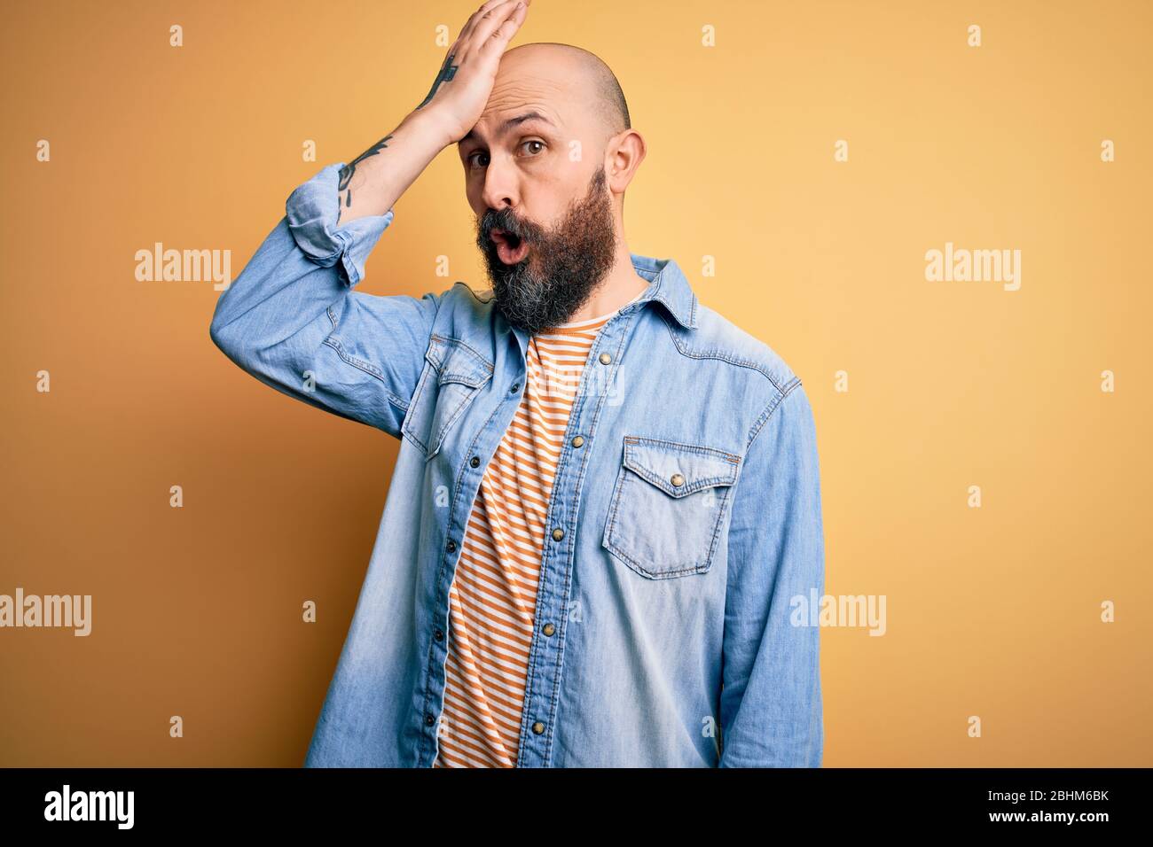 Handsome bald man with beard wearing casual denim jacket and striped t ...