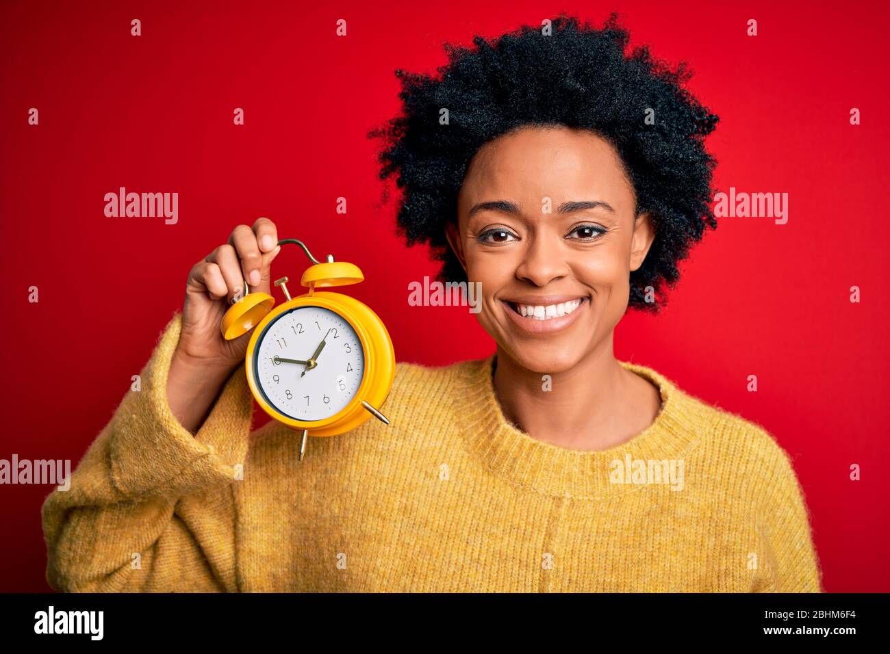 Young African American afro woman with curly hair holding vintage alarm ...
