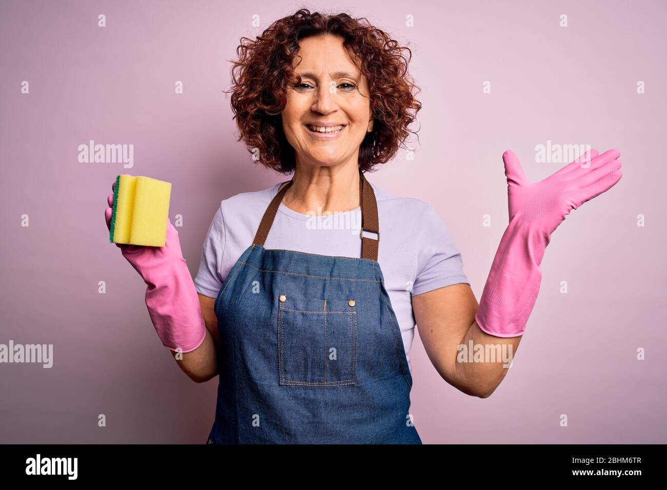 Middle age curly hair woman cleaning doing housework wearing apron and ...