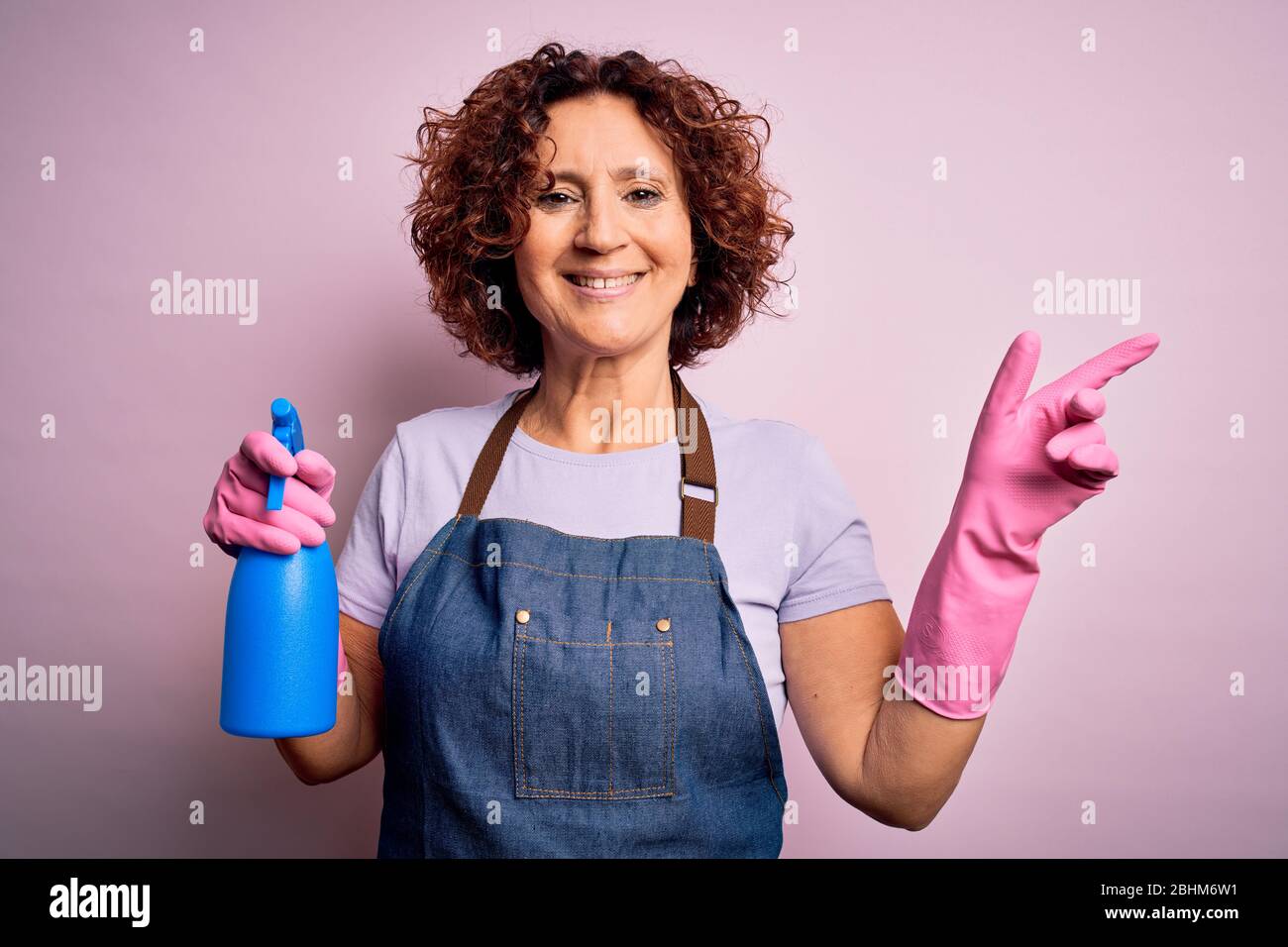 Middle age curly hair woman cleaning doing housework wearing apron and ...