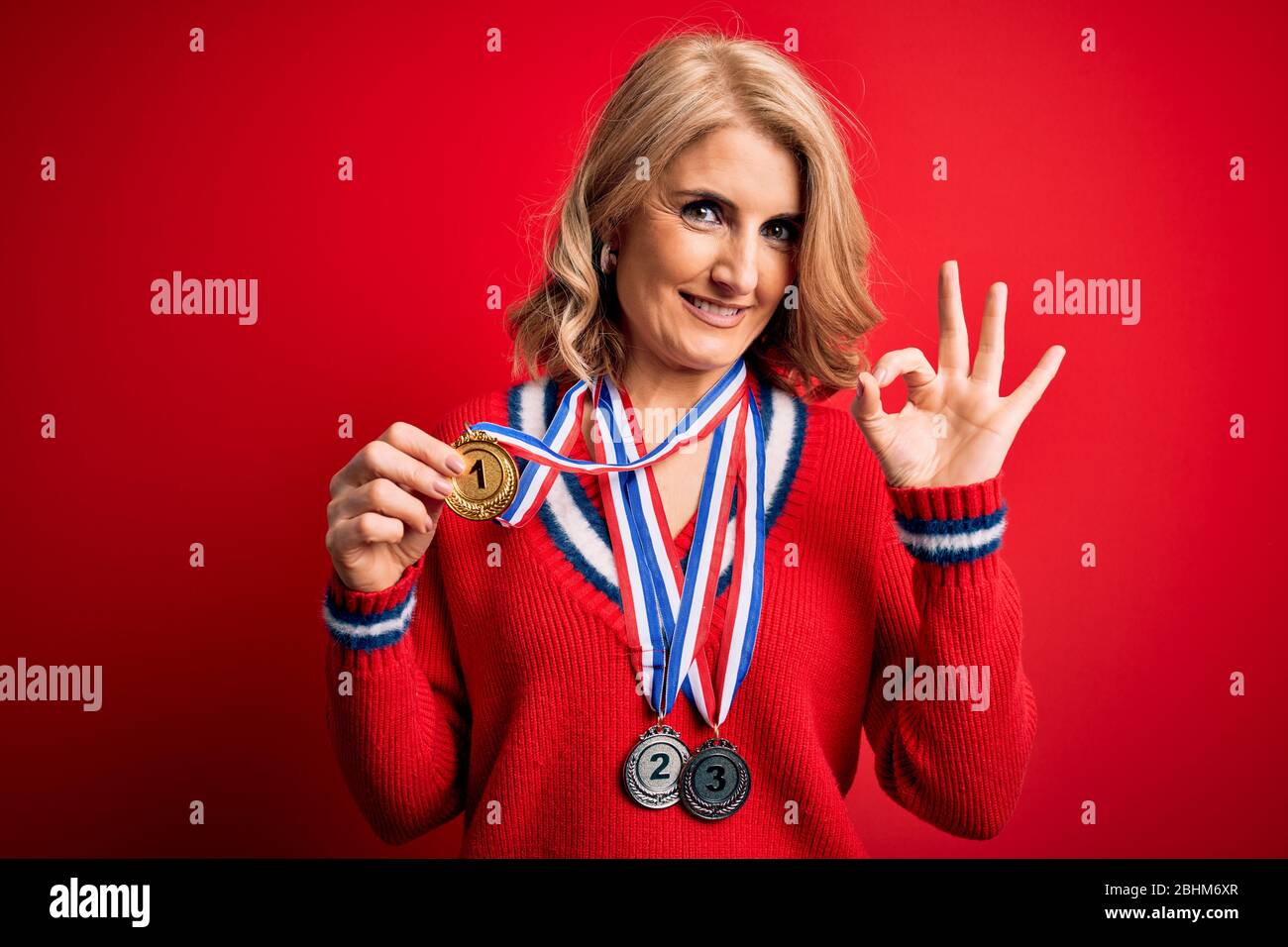 Middle age beautiful blonde successful woman winning medals over red ...