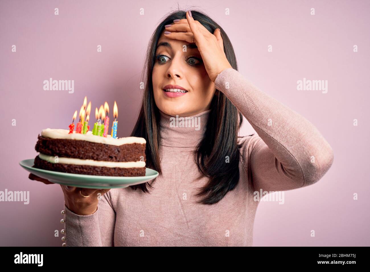 Young woman with blue eyes holding birthday cake with candles over pink ...
