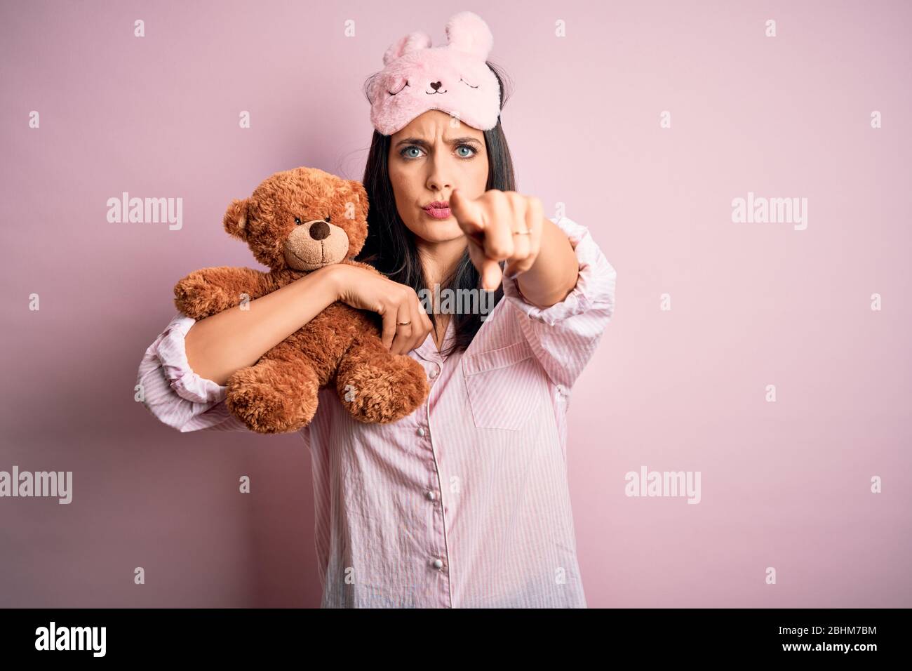 Young brunette woman with blue eyes wearing pajama hugging teddy bear ...