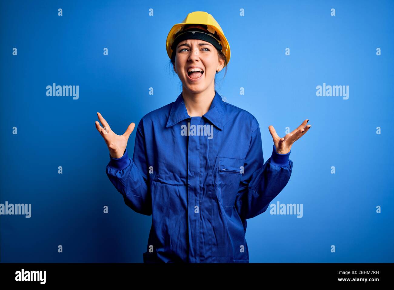 Young beautiful worker woman with blue eyes wearing security helmet and ...
